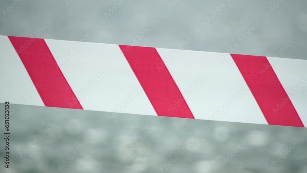 Red white warning tape barrier ribbon swinging in the wind across ...