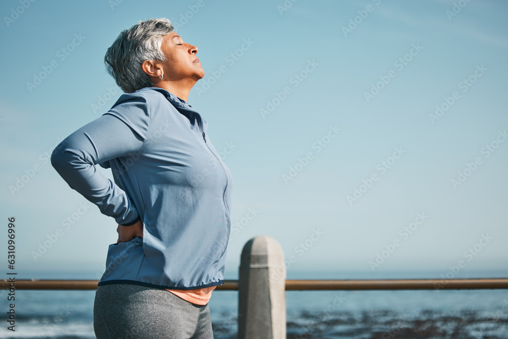 Tired, running and senior woman pain from back ache by the ocean for ...
