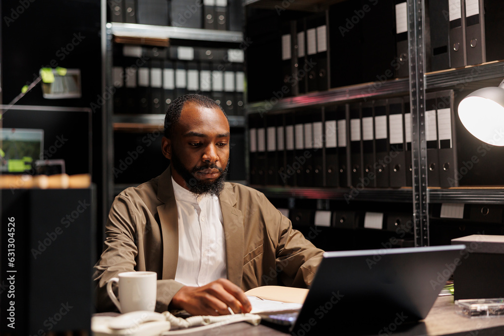 African american cop working overtime on laptop in dark detective ...