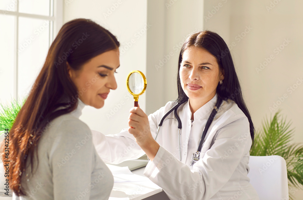 Female friendly doctor examining face skin of young smiling woman ...