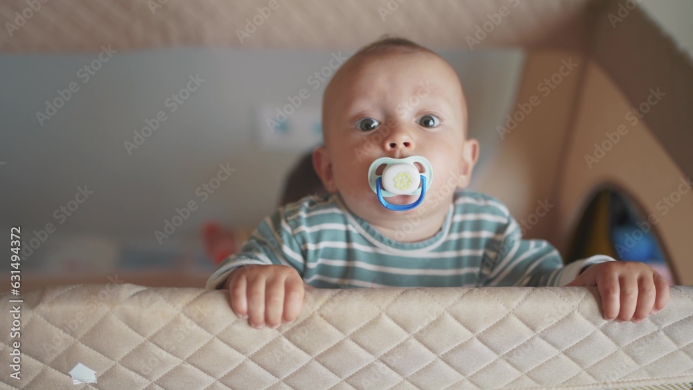 baby with a pacifier in his mouth is in the crib arena looking at the ...