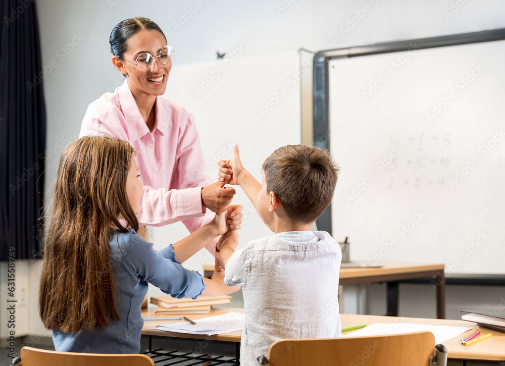 Happy children and educator raising hands up sitting at table in modern ...
