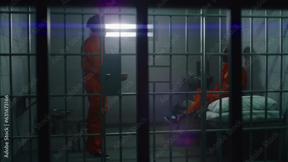 Two African American prisoners in orange uniforms talk. One man sits on ...