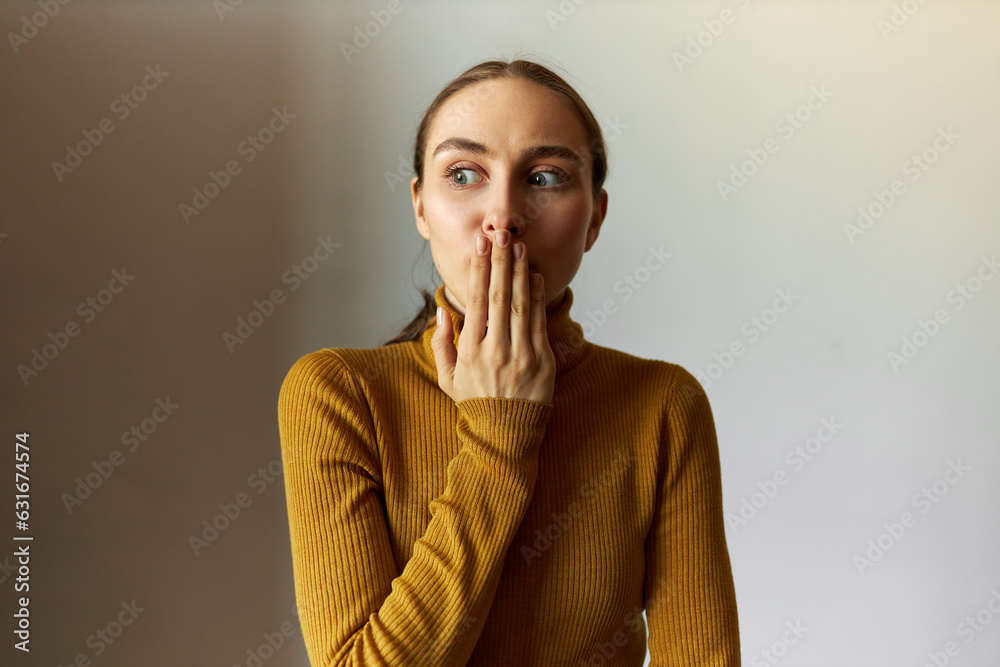 Portrait of shocked female in yellow clothes covering mouth with scared ...
