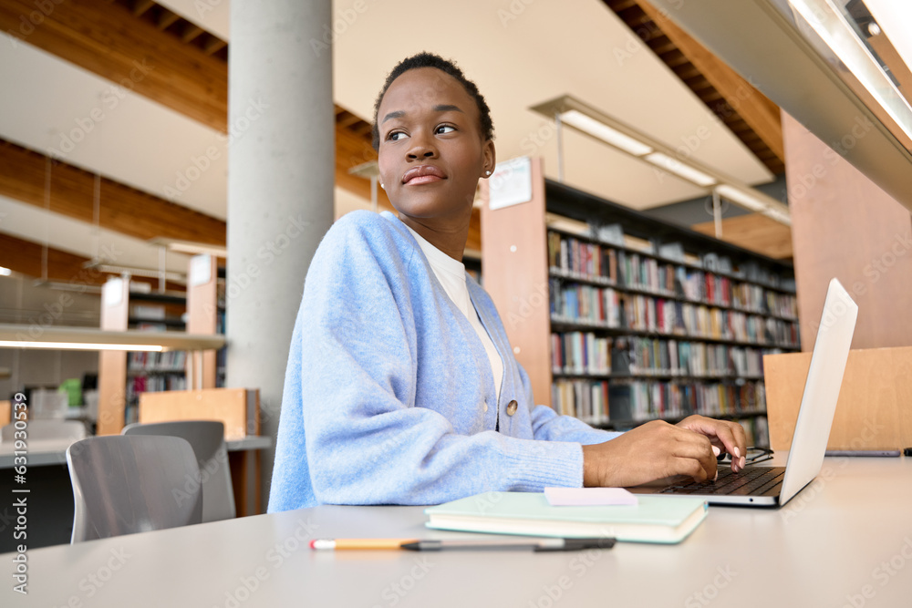 African Black girl student studying in university library using laptop ...