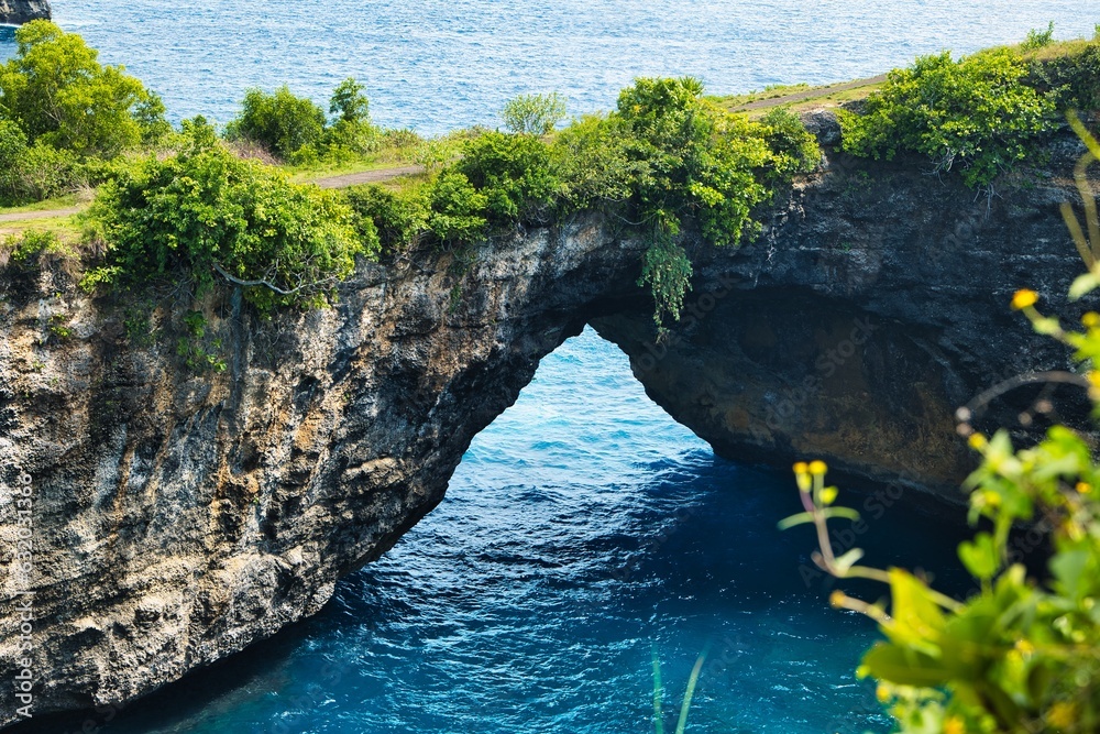 Overgrown stone arch bridge of Broken Beach in Nusa Penida. Lush green ...