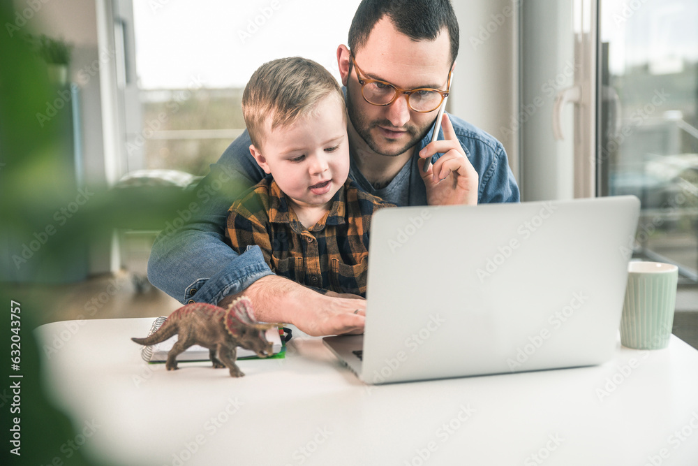 Father working at table in home office with son sitting on his lap ...