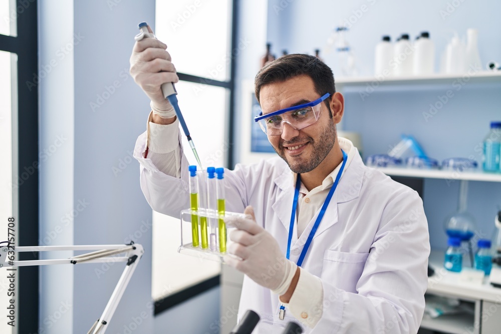 Young hispanic man scientist measuring liquid using pipette at ...