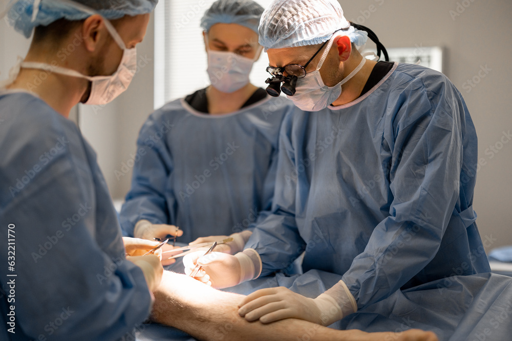 Three confident surgeons performing surgical operation on a patient's ...