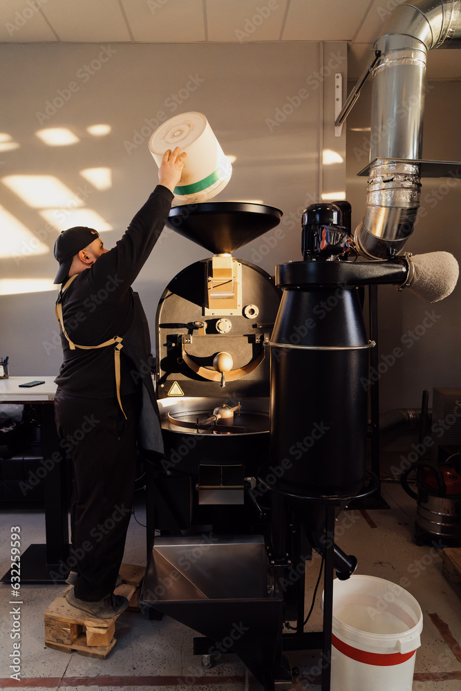 Side view of male worker in uniform and cap pouring raw coffee beans ...