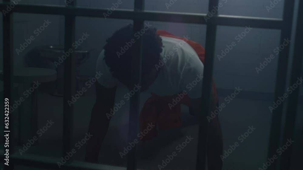 African American prisoner in orange uniform does push-ups and shadow ...