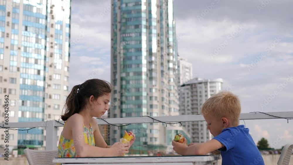Two hungry children are eating street food in a summer cafe, a girl is ...