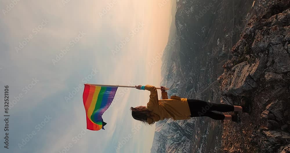 Side view of female in a mountain waving LGBT Pride flag. Woman holding ...