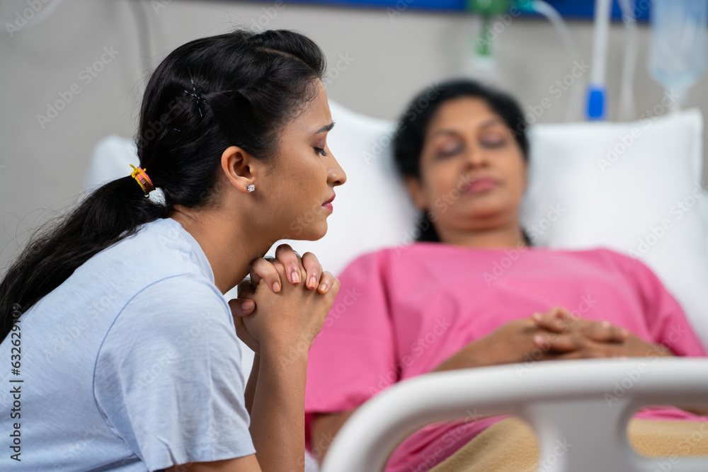 worried indian daughter praying for sick admitted mother for health recovery at hospital ...