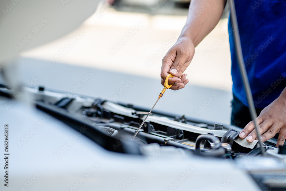 Auto mechanic repairman using tablet and pulling dipstick to checking ...