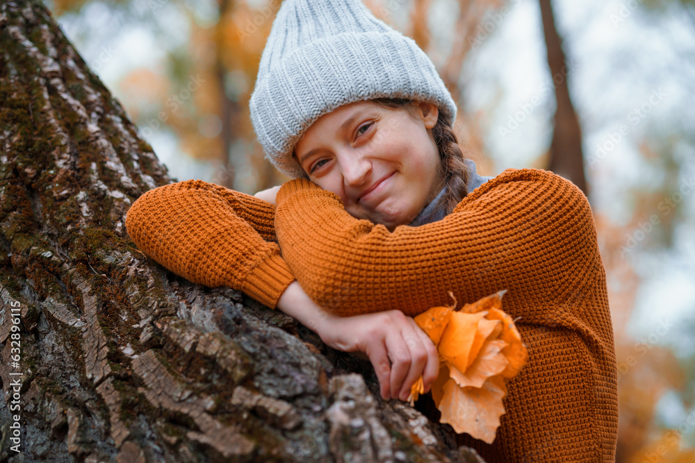 a young teenage girl posing in an autumn forest, standing by a tree ...