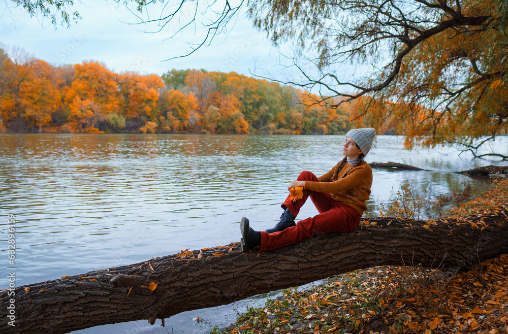 a young teenage girl posing in an autumn forest, sitting on a tree by ...