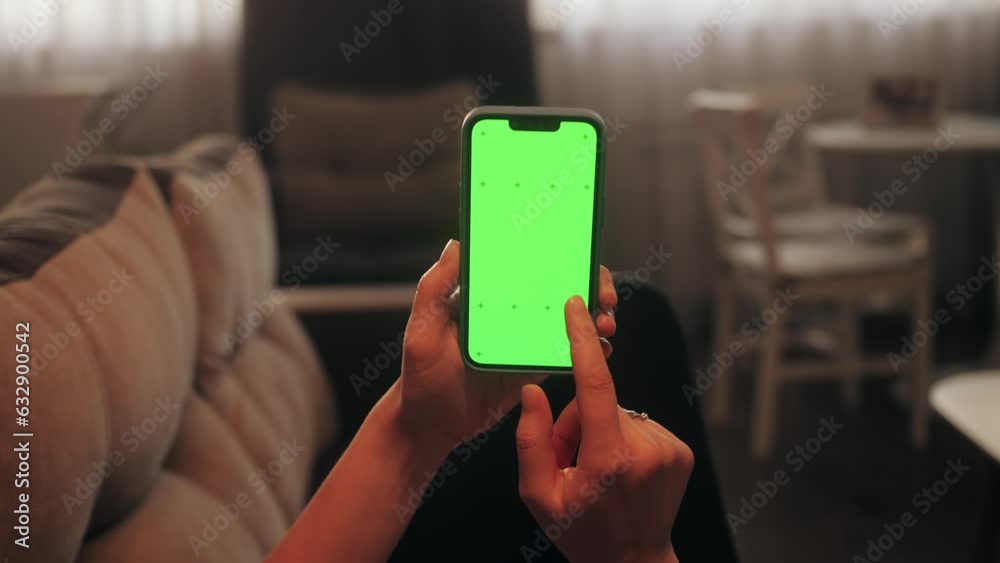 Woman lying on sofa in modern cozy living room using smartphone with chroma key green screen ...