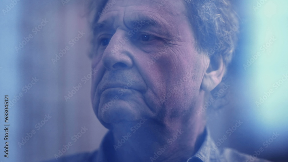 Brooding senior man lost in thought, gazing through his window as the ...