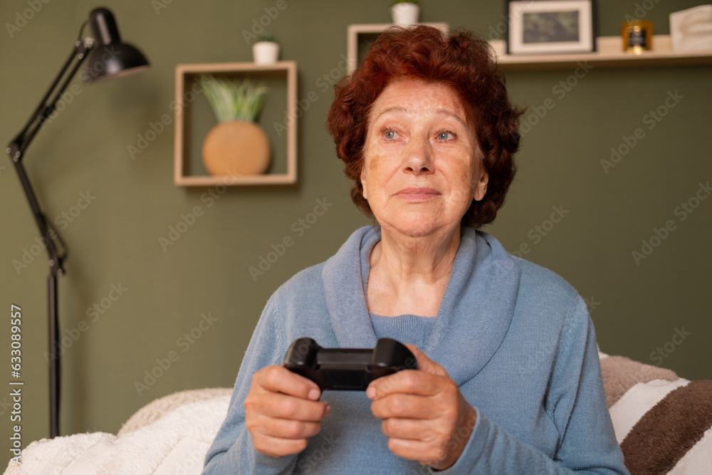 A modern elderly woman sits on a sofa in a room and plays a computer ...
