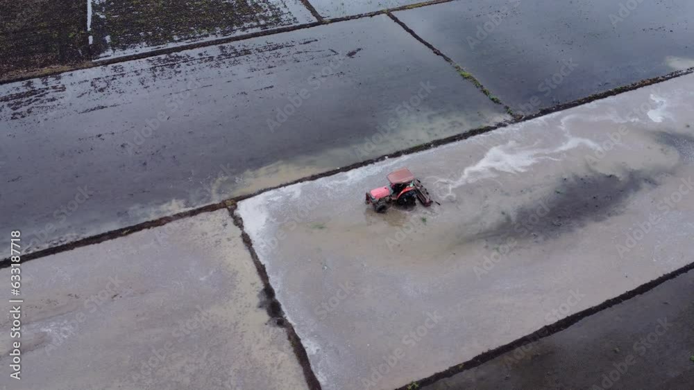Aerial view of farmer in red tractor preparing land for rice planting ...