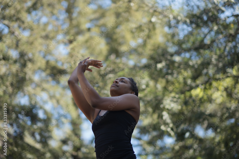A person stretches outdoors, and is mid-pose with their arms arched ...