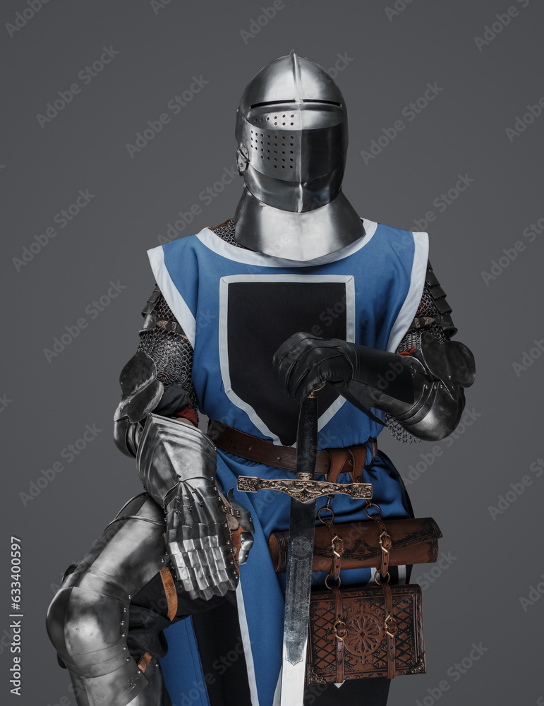 Regal knight stands leaning on his sword, dressed in medieval armor ...
