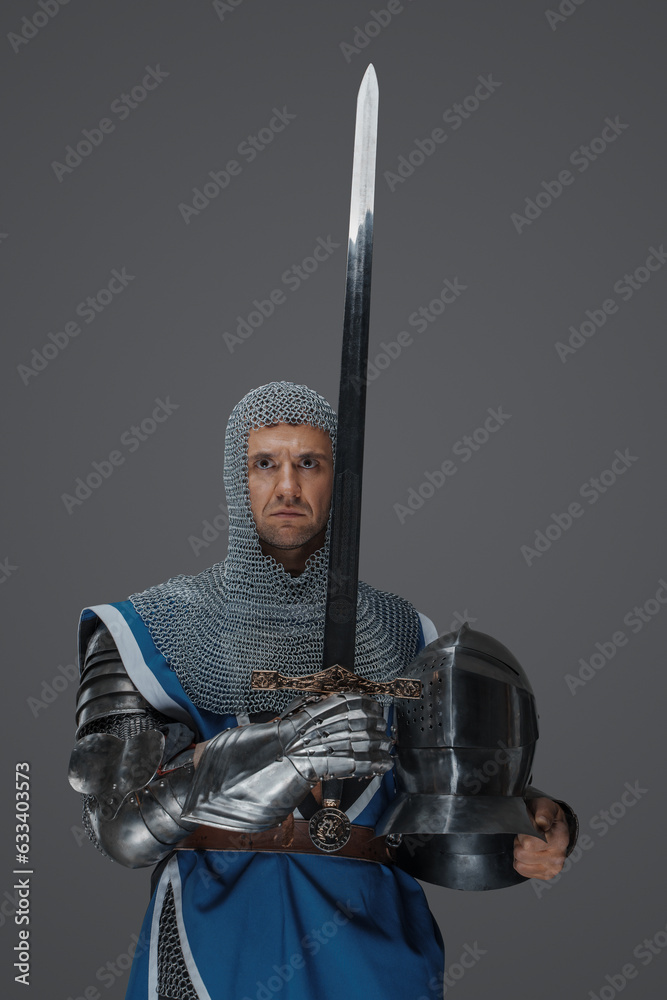 Proud knight stands holding his sword and helmet, donning blue surcoat ...
