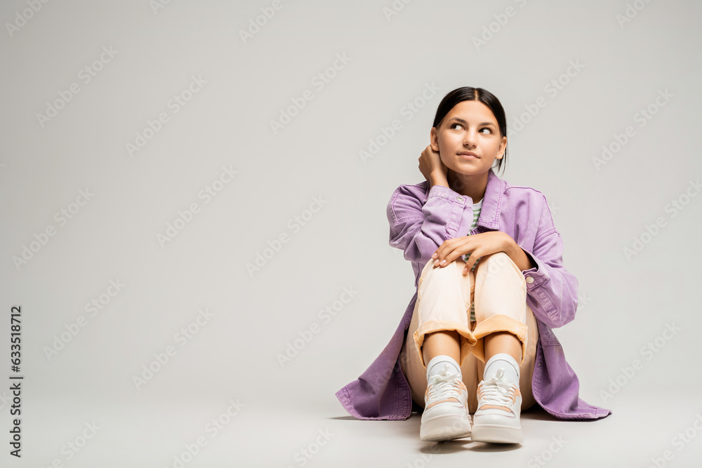 Teenage girl sits on floor with legs tucked up to chest and looks ...