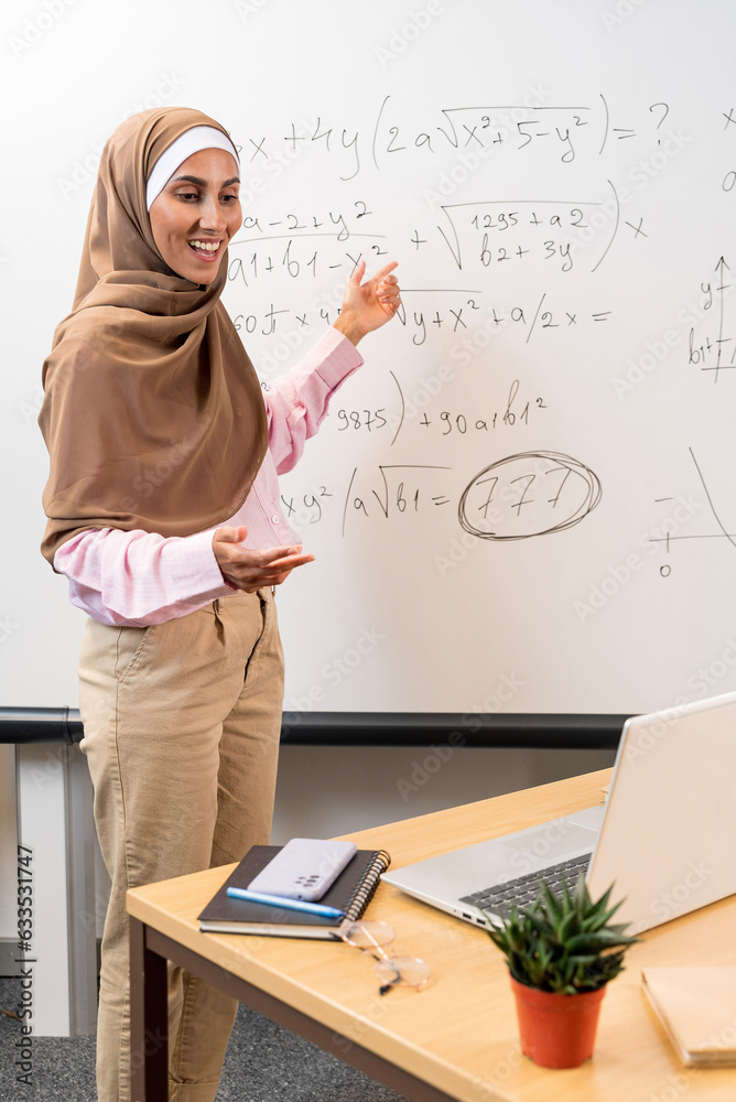 Young Middle Eastern teacher in a hijab explains a lesson online ...