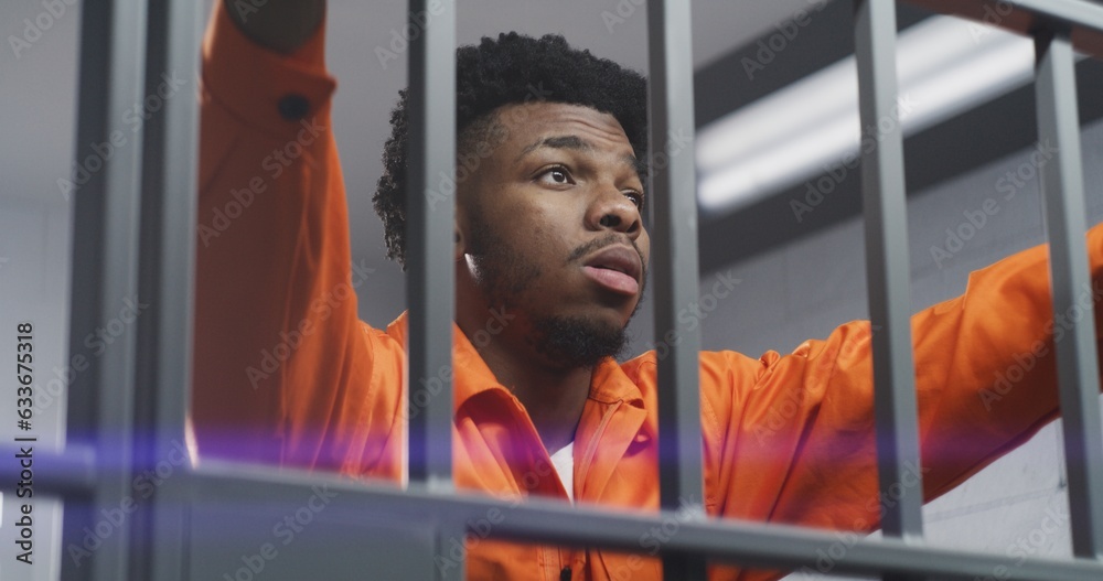 Sad African American man in orange uniform leans hands on prison cell ...