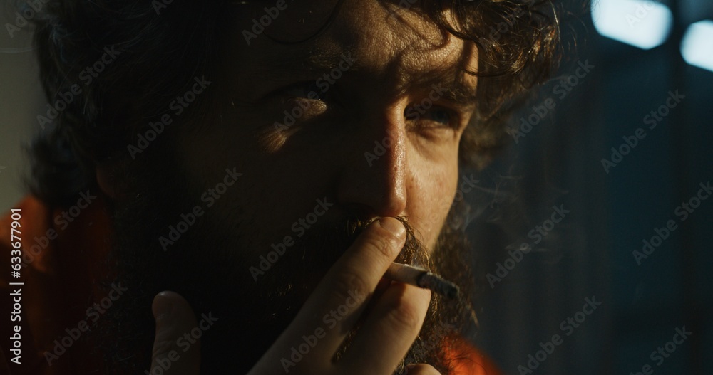Depressed male prisoner in orange uniform sits in prison cell, smokes ...