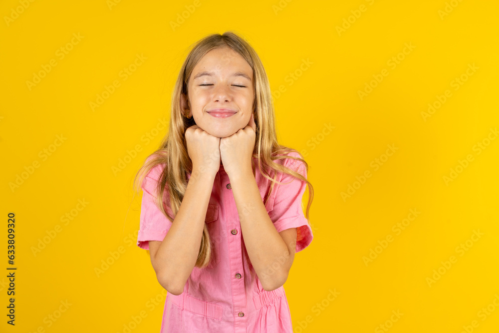 Cheerful young beautiful blonde kid girl over yellow studio background ...