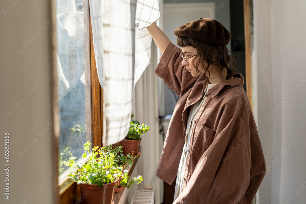 Pensive tired young woman, pulling back curtain in social isolation, no ...
