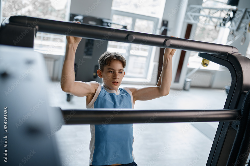 Teenager boy pulling up on crossbar closeup shot over gym background ...