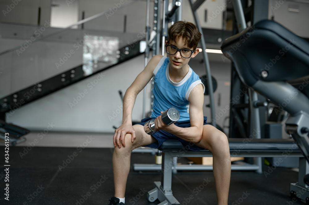 Skinny nerd boy doing lifting workout with dumbbells training at gym ...