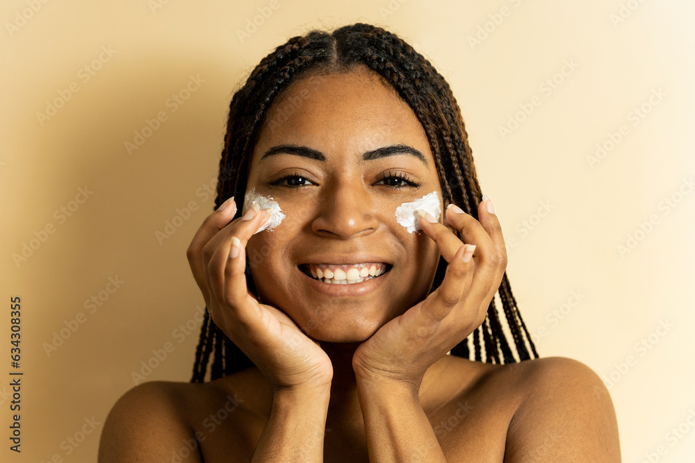 African woman with braided hair applies cream on both sides of her face ...