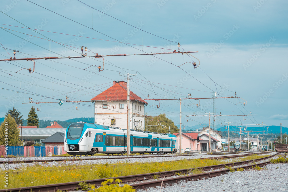 Passenger train in white and blue is rushing through the station of Ljubljana Vizmarje on a ...