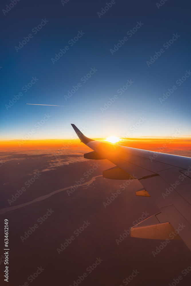 Airplane flight in sunset sky over ocean water and wing of plane. View ...