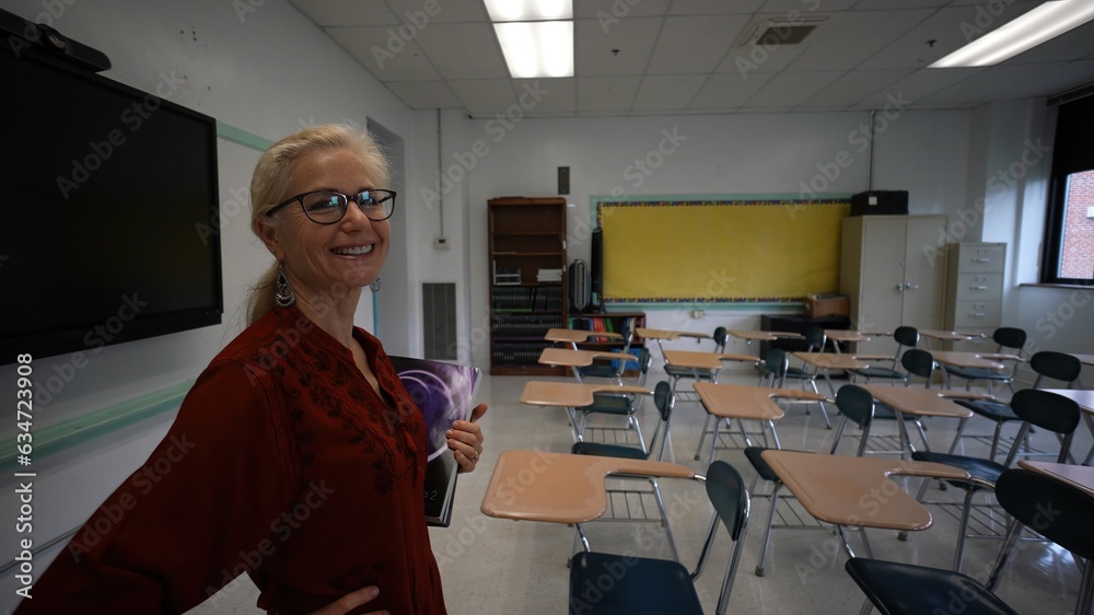 Portrait of smiling happy teacher entering an empty classroom, turning ...