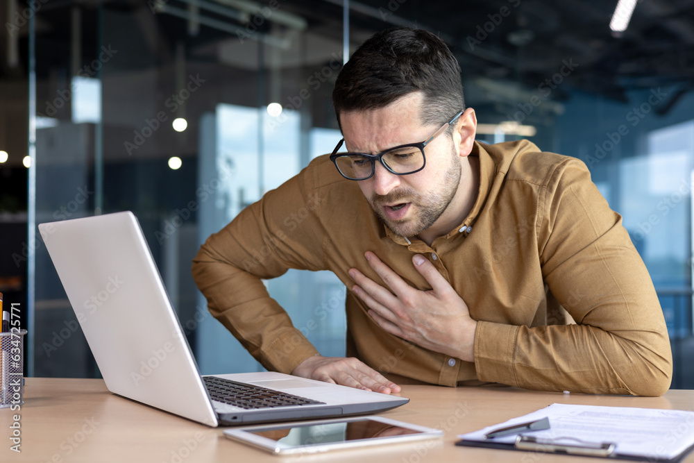 Heart attack, panic attack at work. A young man holds his chest while ...