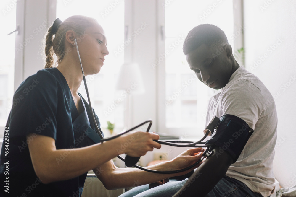 Female nurse checking blood pressure of male teenage patient sitting in ...