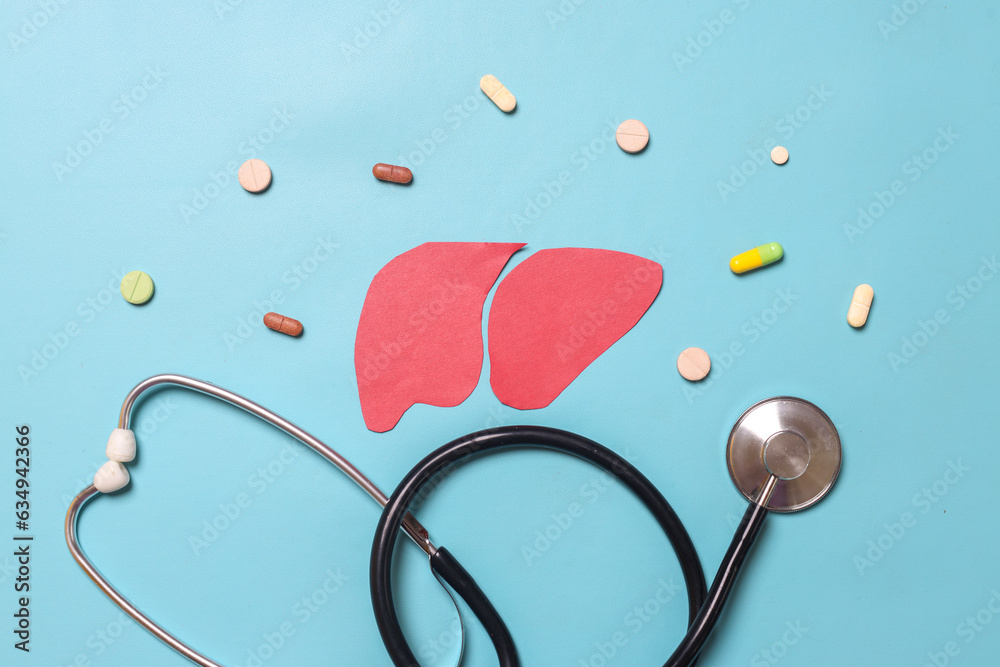 Human liver organ, stethoscope and various pills over blue background ...