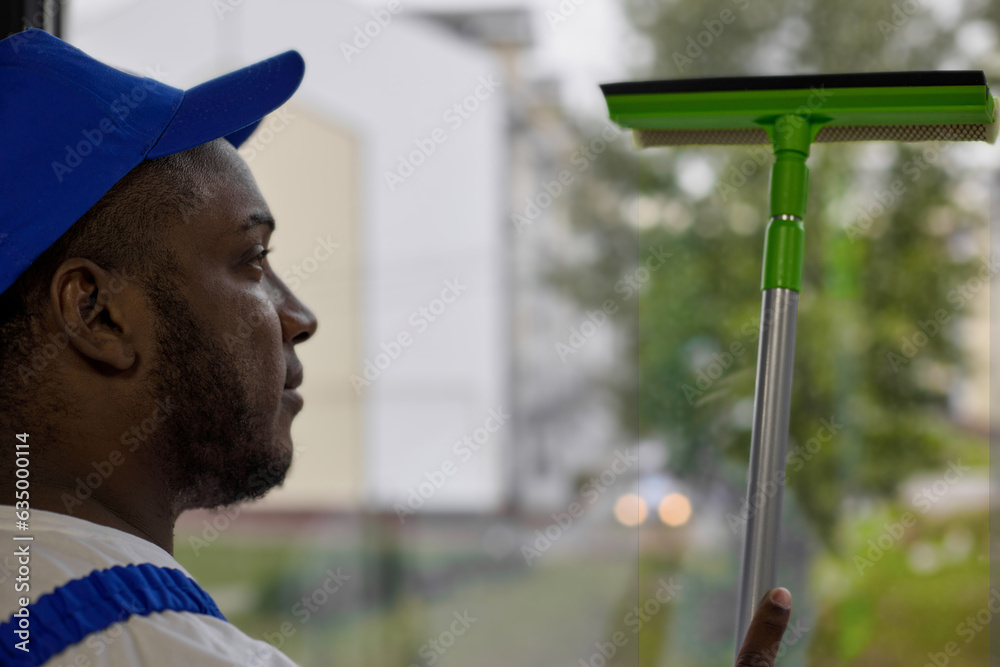 Black guy thoroughly washes a dusty office window. Photo from the back ...