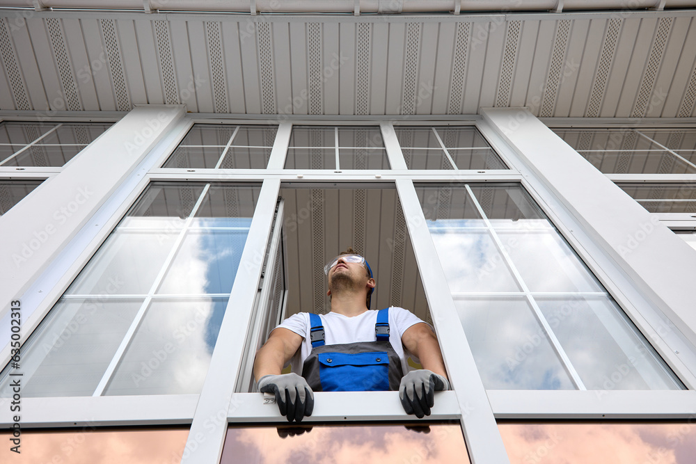 Worker in blue overalls and gloves stands at an open window, looking ...