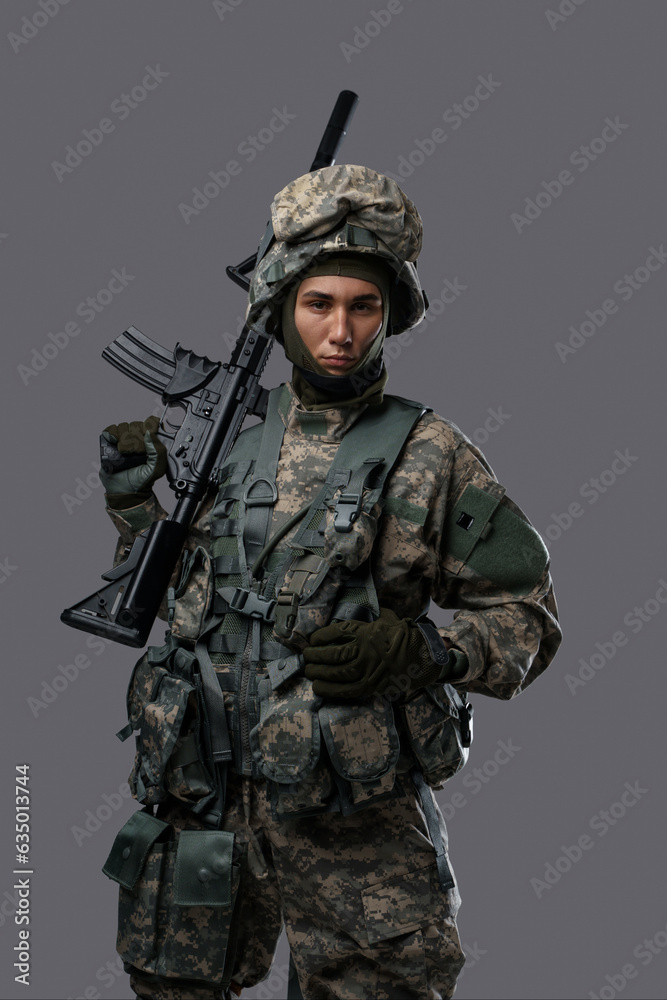 Young soldier poses with a serious expression on a plain grey ...