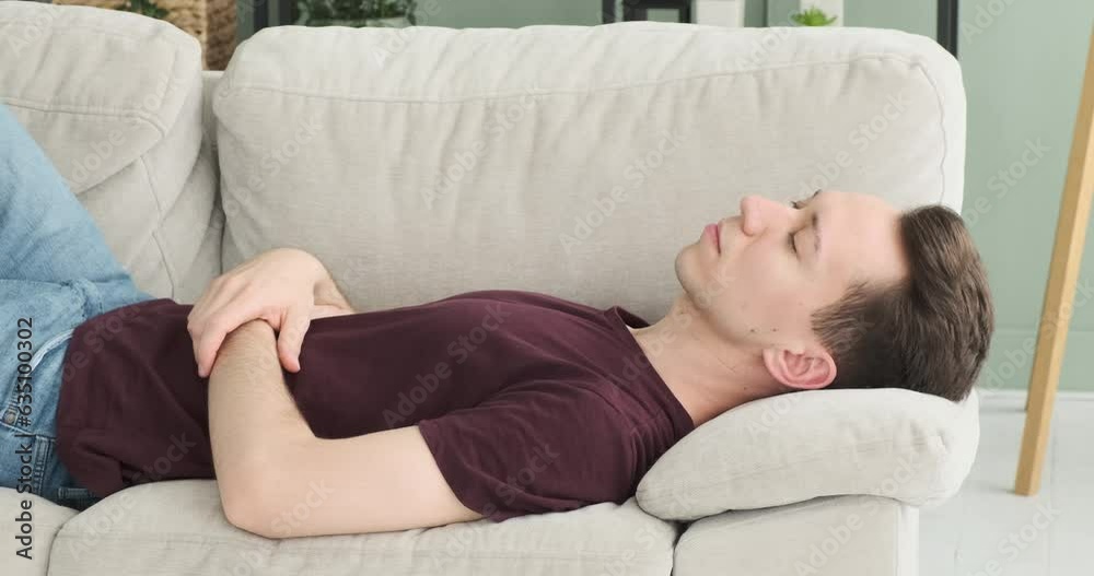 In this peaceful scene, a young man is captured dozing off on the sofa ...