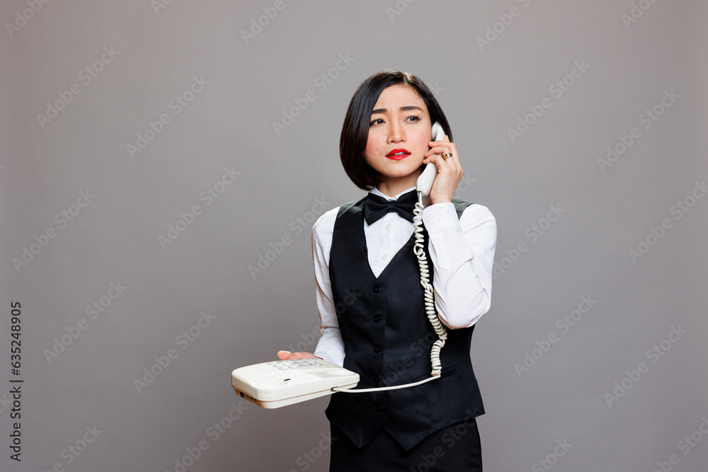 Young confident asian waitress in uniform talking on landline phone and ...