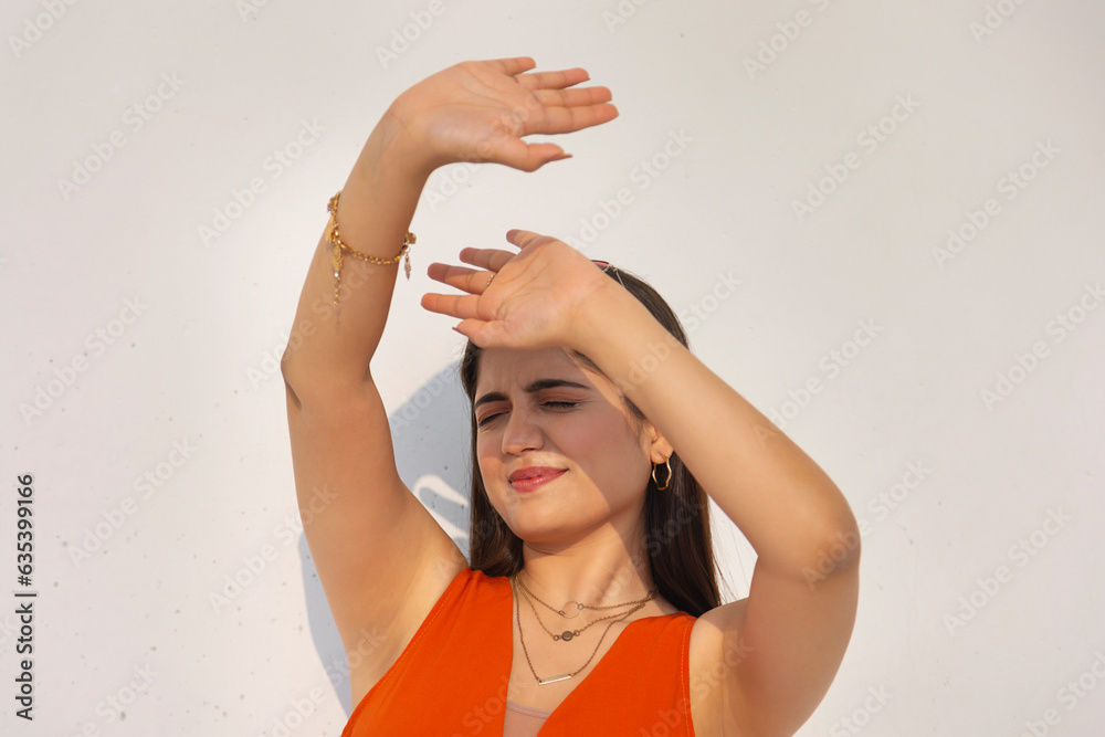 Woman covering her face from sun with her hand while standing against ...