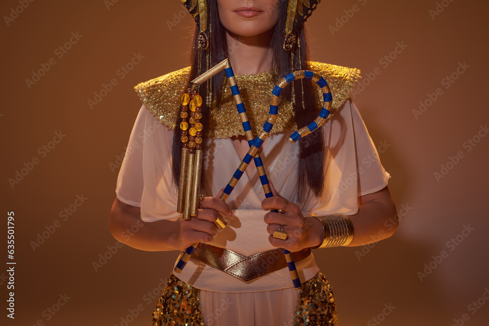 Cropped view of woman in egyptian look holding crook and flail on brown ...